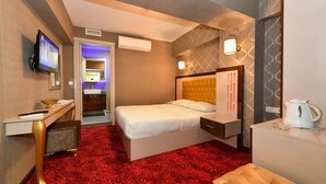 Quarto de hotel com cama, mesa de cabeceira, televisão e tapete vermelho.