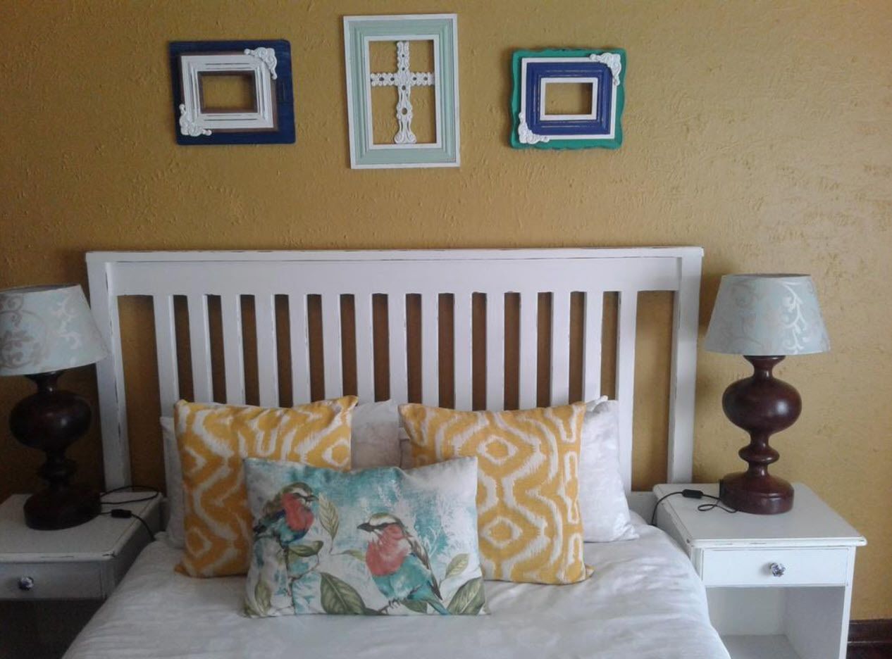 Uma cama com cabeceira branca, duas mesas de cabeceira com luminárias e arte decorativa na parede.