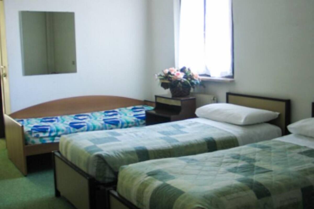 Quarto com duas camas, mesa de cabeceira com um vaso de flores e janela com cortinas.