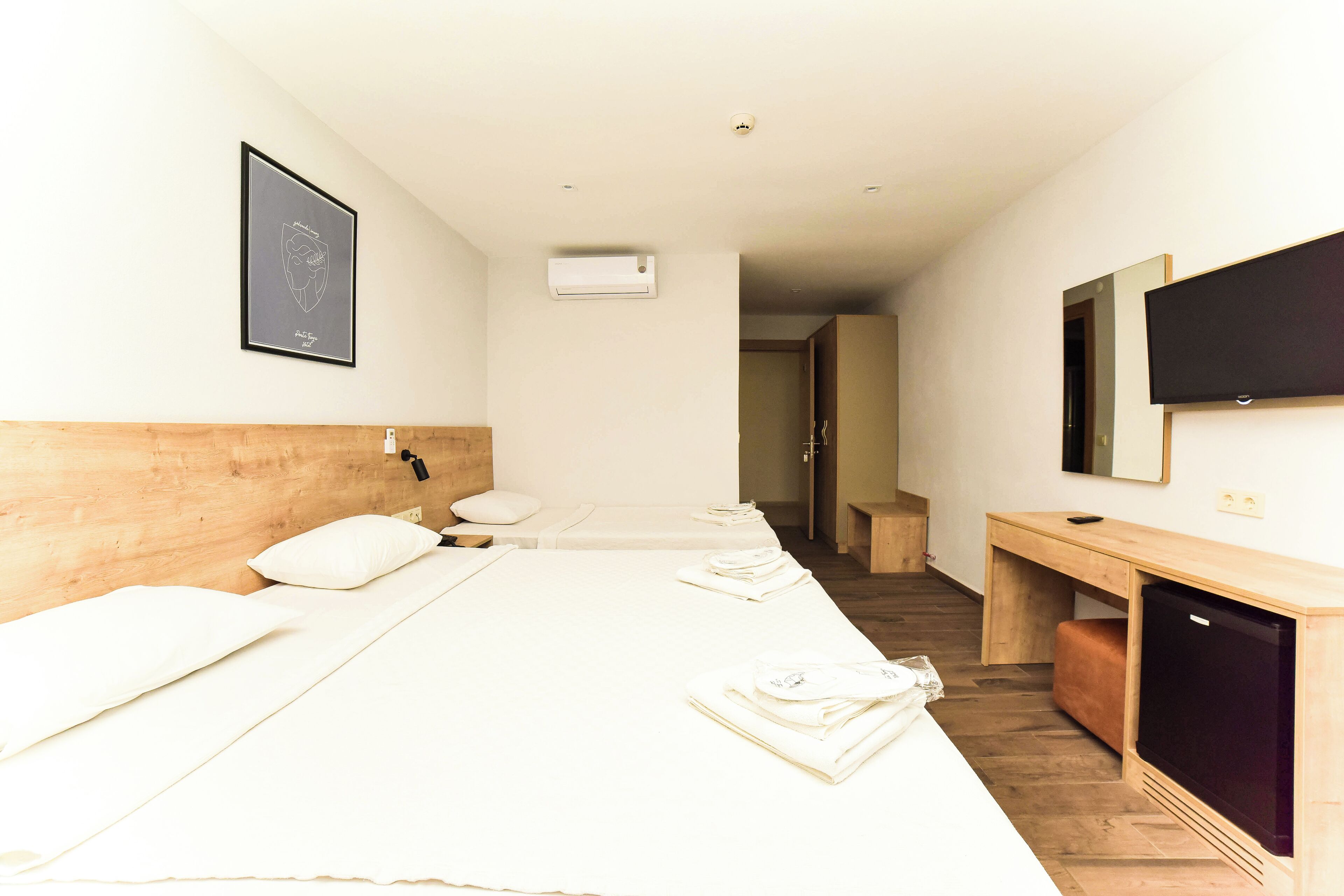 Quarto de hotel com cabeceira de madeira, cama com roupa de cama branca, escrivaninha com televisão de tela plana e quadro na parede.