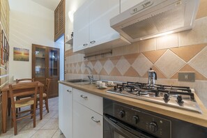 Cozinha com fogão a gás, armários brancos, mesa de jantar de madeira com cadeiras e painel de azulejos.
