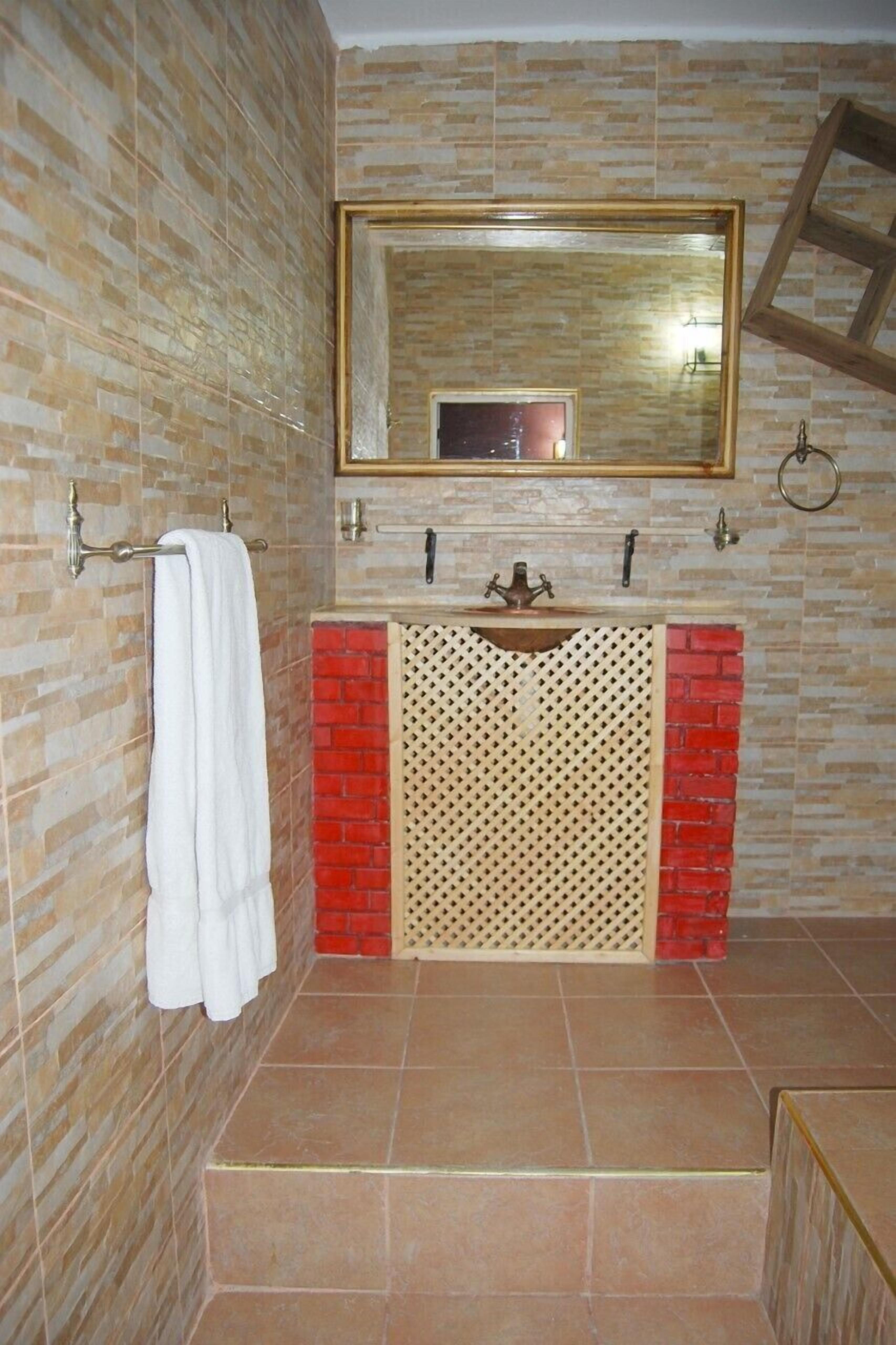 Uma casa de banho com parede revestida a azulejos, uma pia com painel de madeira e uma toalha pendurada num suporte de metal.