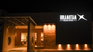Exterior do Hotel Uramutam Palace, com uma placa visível, área de recepção e escadaria que leva à entrada.