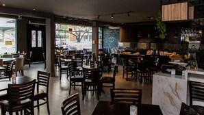 Um restaurante moderno com área de bar, diversas opções de assentos e cozinha à vista.