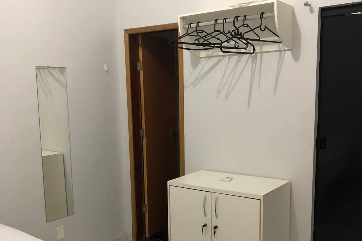 Quarto com cama, armário branco, espelho e cabideiro.
