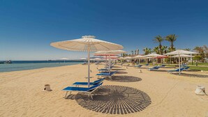 Uma praia com fileiras de espreguiçadeiras e guarda-sóis, céu claro e mar calmo.