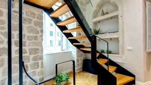 Uma escadaria moderna com degraus de madeira e corrimãos pretos, que leva a um patamar com uma planta em vaso e uma prateleira com objetos decorativos.