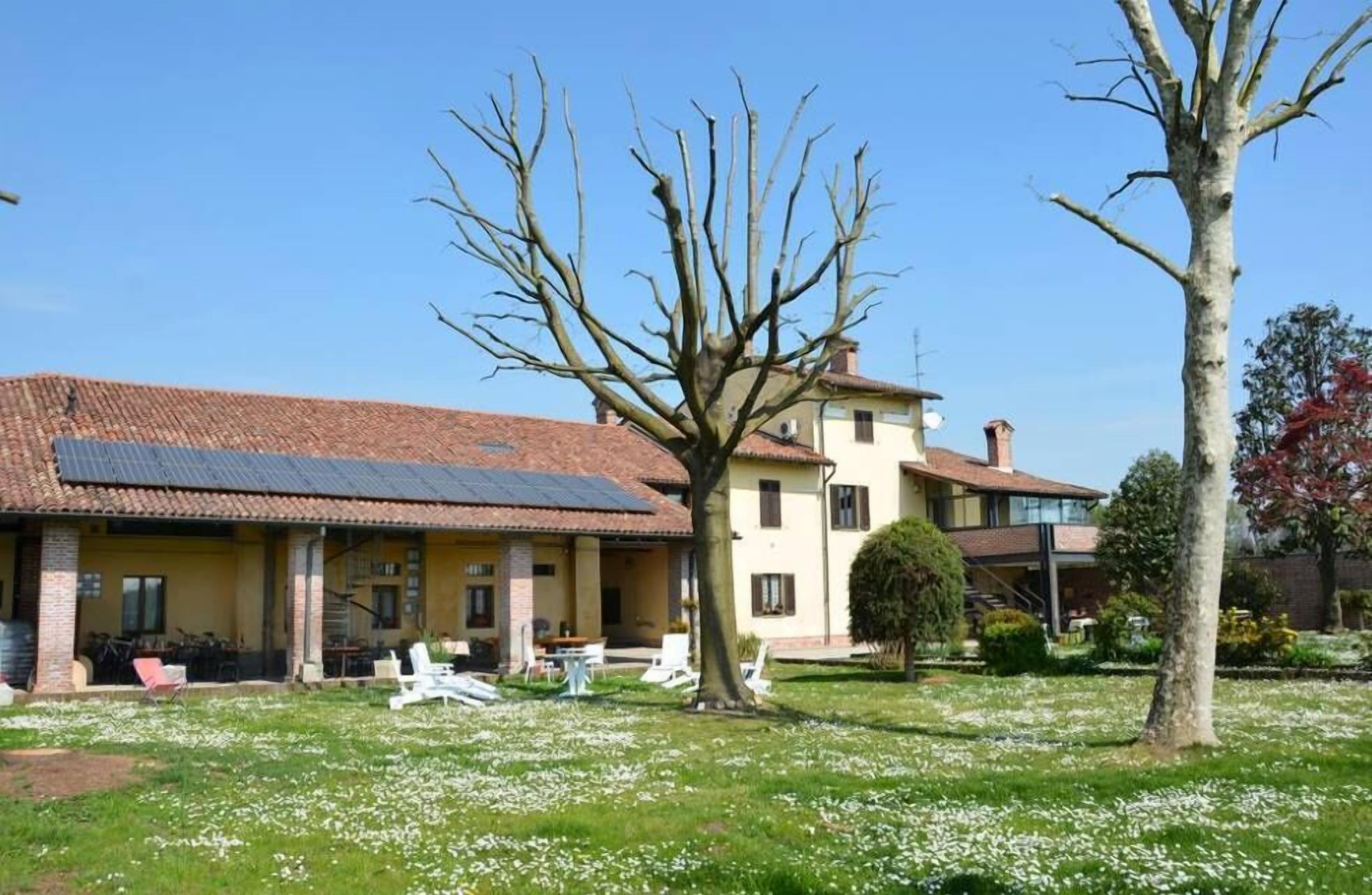 Um edifício de dois andares com telhado telhado, varanda coberta e jardim com flores brancas.