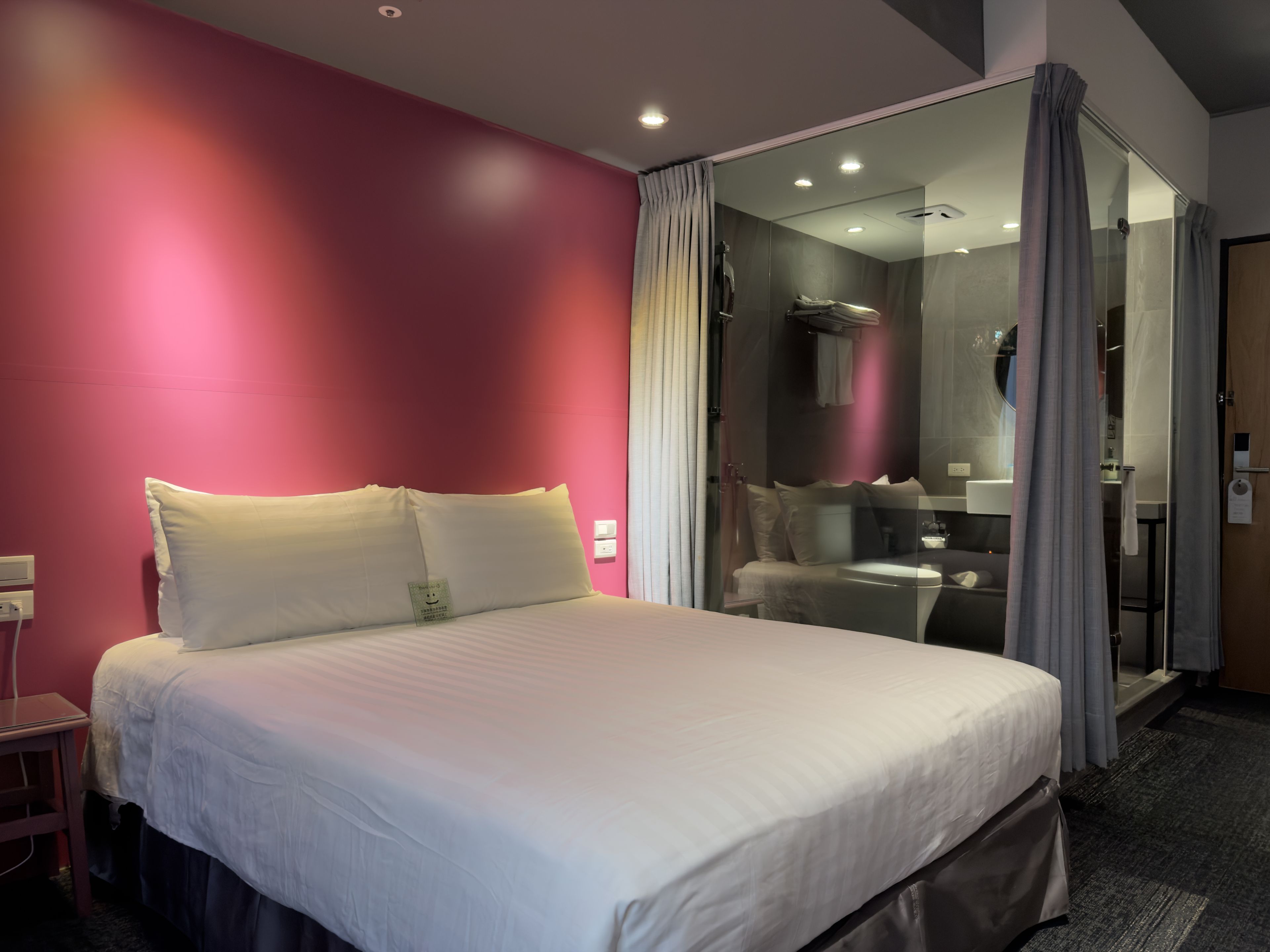 Quarto de hotel moderno com uma cama grande, divisória de vidro e banheiro com chuveiro.