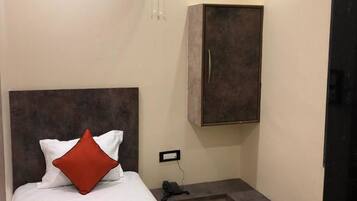 Quarto com cama, mesa de cabeceira, escrivaninha, guarda-roupa, ventilador e janela.