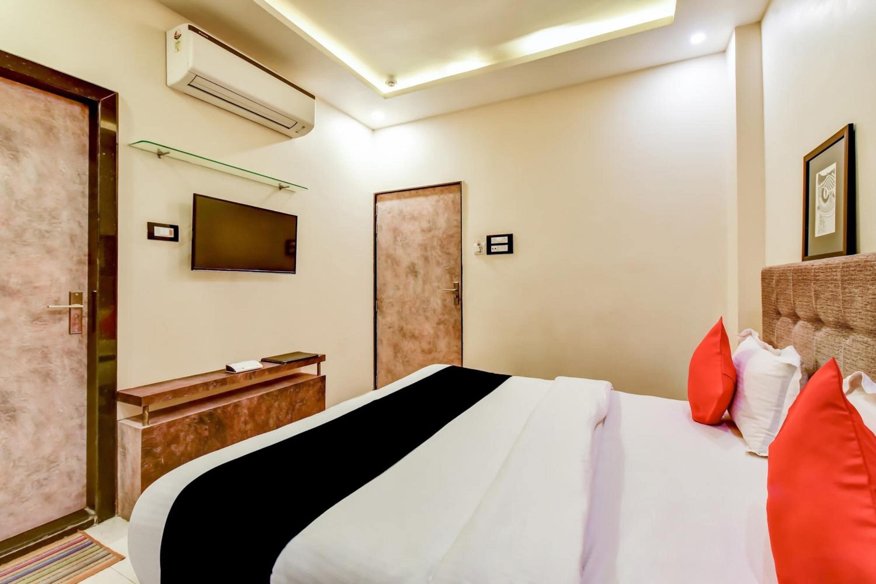 Quarto de hotel com cama, escrivaninha, televisão e ar condicionado.