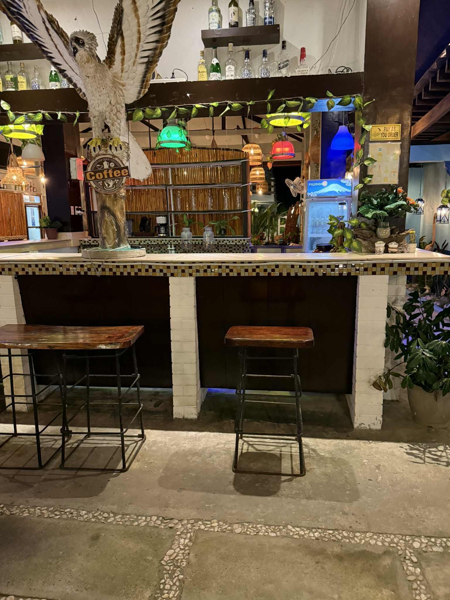 Uma área de bar com sinalização de café, banquetas e diversas garrafas em prateleiras.