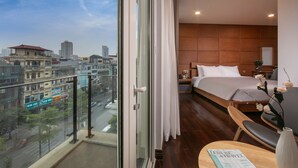 Quarto de hotel moderno com uma varanda grande, uma cama, uma escrivaninha e vista para a paisagem urbana.