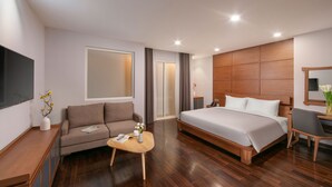 Quarto de hotel moderno com piso de madeira, uma cama grande, um sofá, uma escrivaninha e uma televisão.
