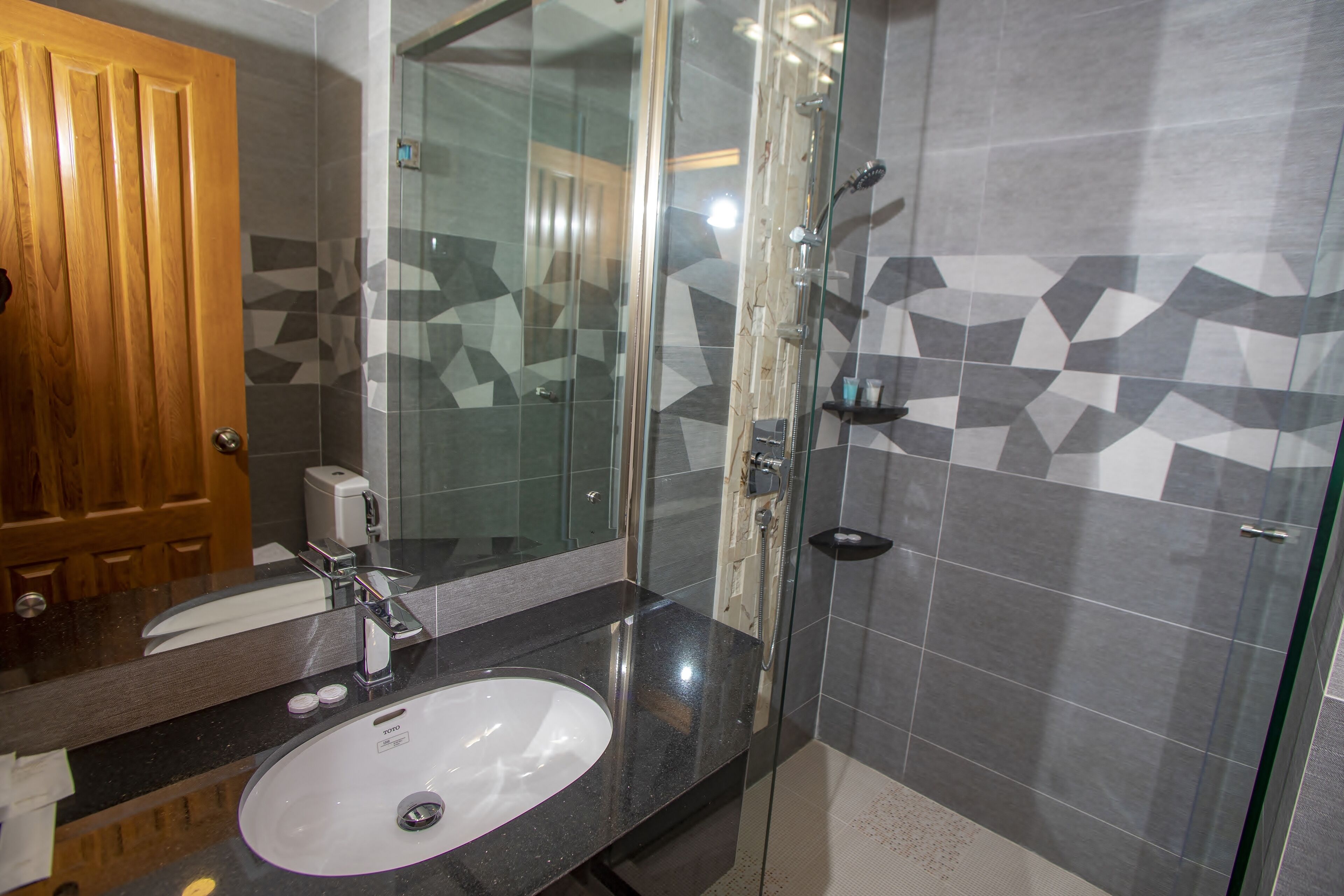 Casa de banho com cabine de duche em vidro, lavatório com espelho e azulejos estampados nas paredes.