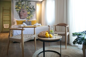 Quarto com uma cama, duas cadeiras, uma mesinha com limões e um copo, e um quadro na parede.