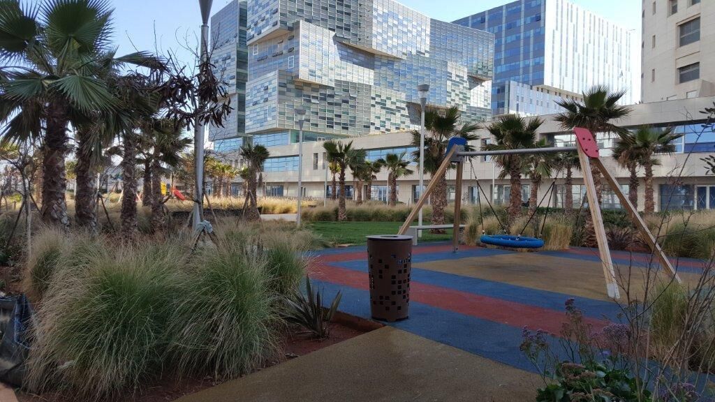 Um parquinho com área de recreação colorida, palmeiras e edifícios modernos ao fundo.