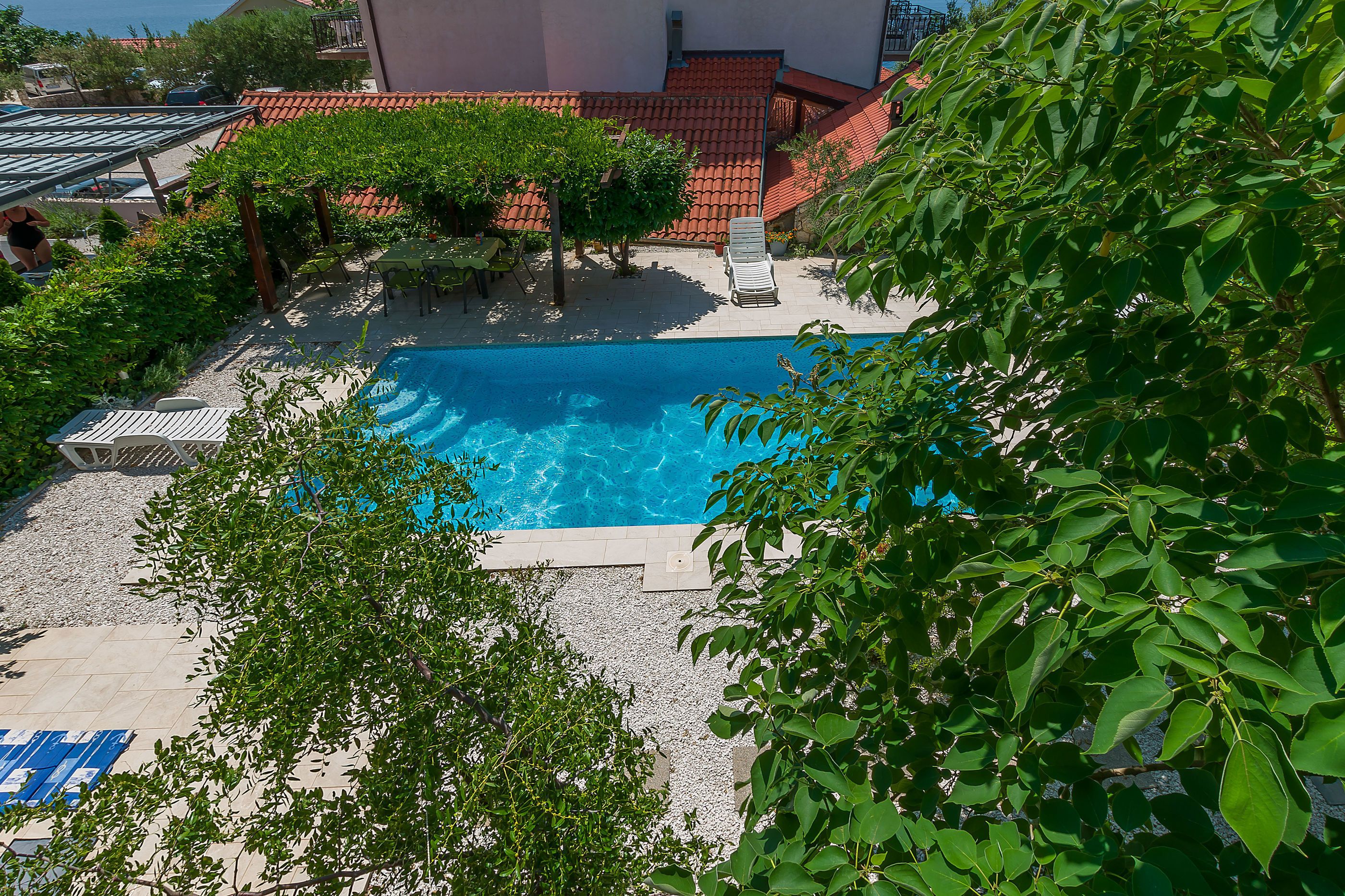 Piscina com espreguiçadeiras, cercada por árvores e um telhado telhado.