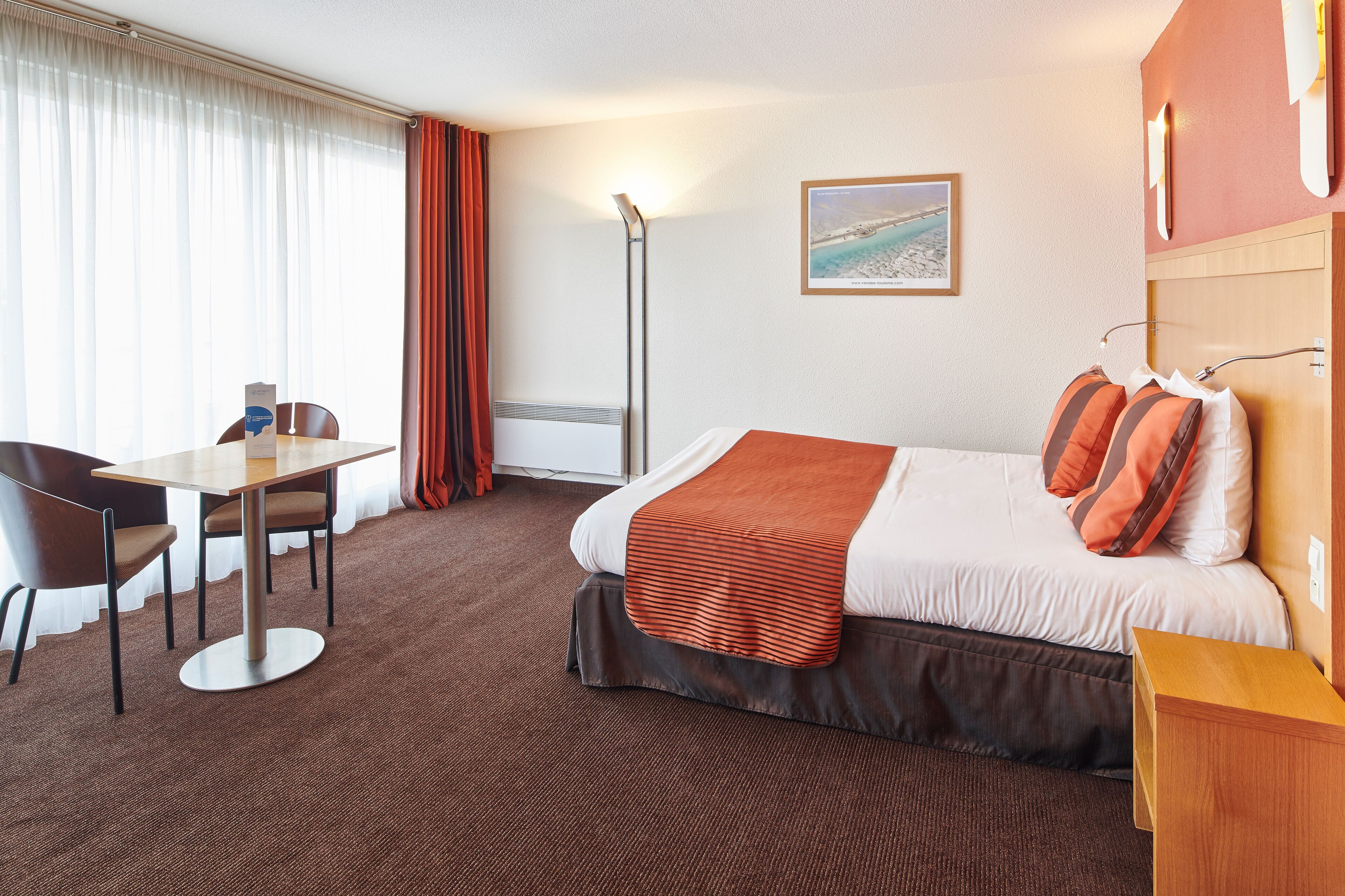 Quarto de hotel com cama, escrivaninha e cadeira.