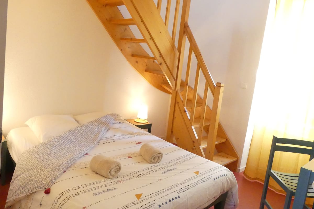 Quarto com escada de madeira, cama com roupa de cama estampada e abajur.