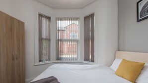 Quarto com cama, janela com persianas, guarda-roupa e um quadro na parede.