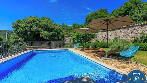 Piscina com muro de pedra, espreguiçadeiras e guarda-sóis.
