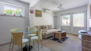 Uma sala de estar moderna com mesa de jantar de vidro, cadeiras amarelas, sofá bege e uma pequena mesa lateral de madeira.