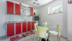 Uma cozinha compacta com armários vermelhos, uma mesa de jantar com tampo de vidro e cadeiras amarelas.