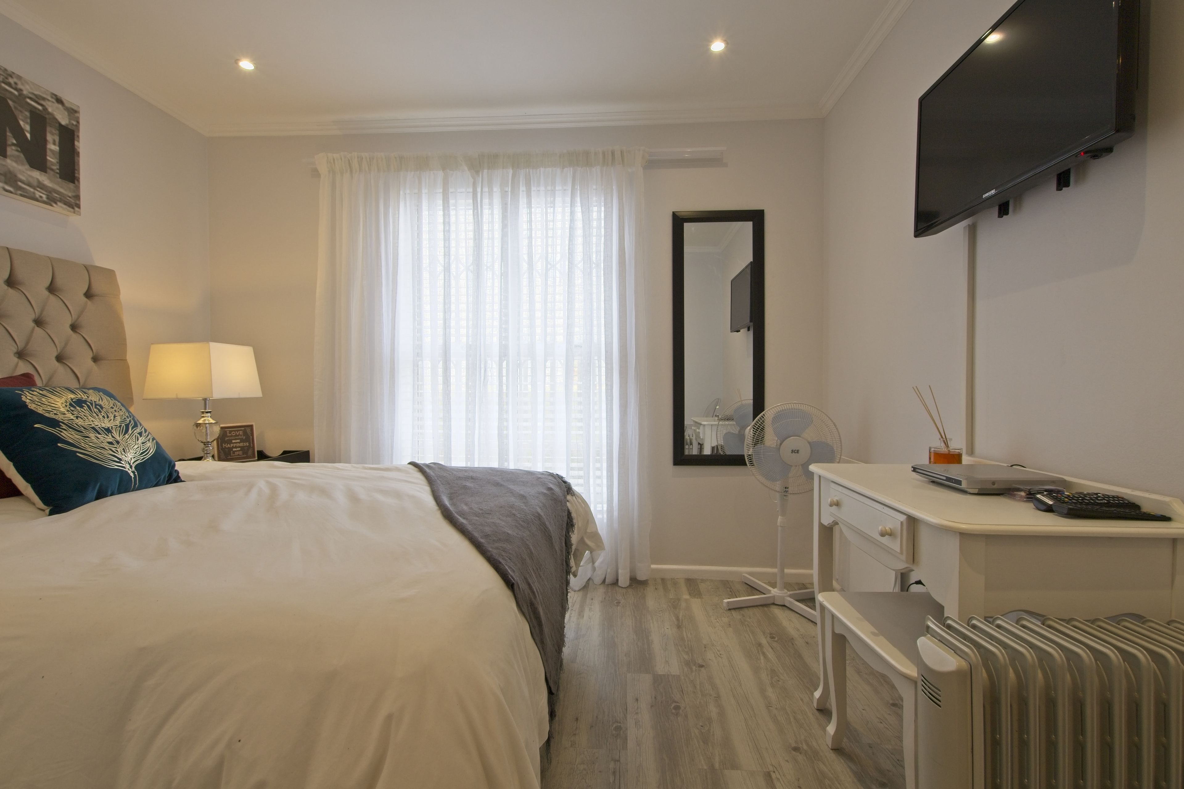 Quarto de hotel com cama, escrivaninha, televisão, espelho e janela com cortinas.
