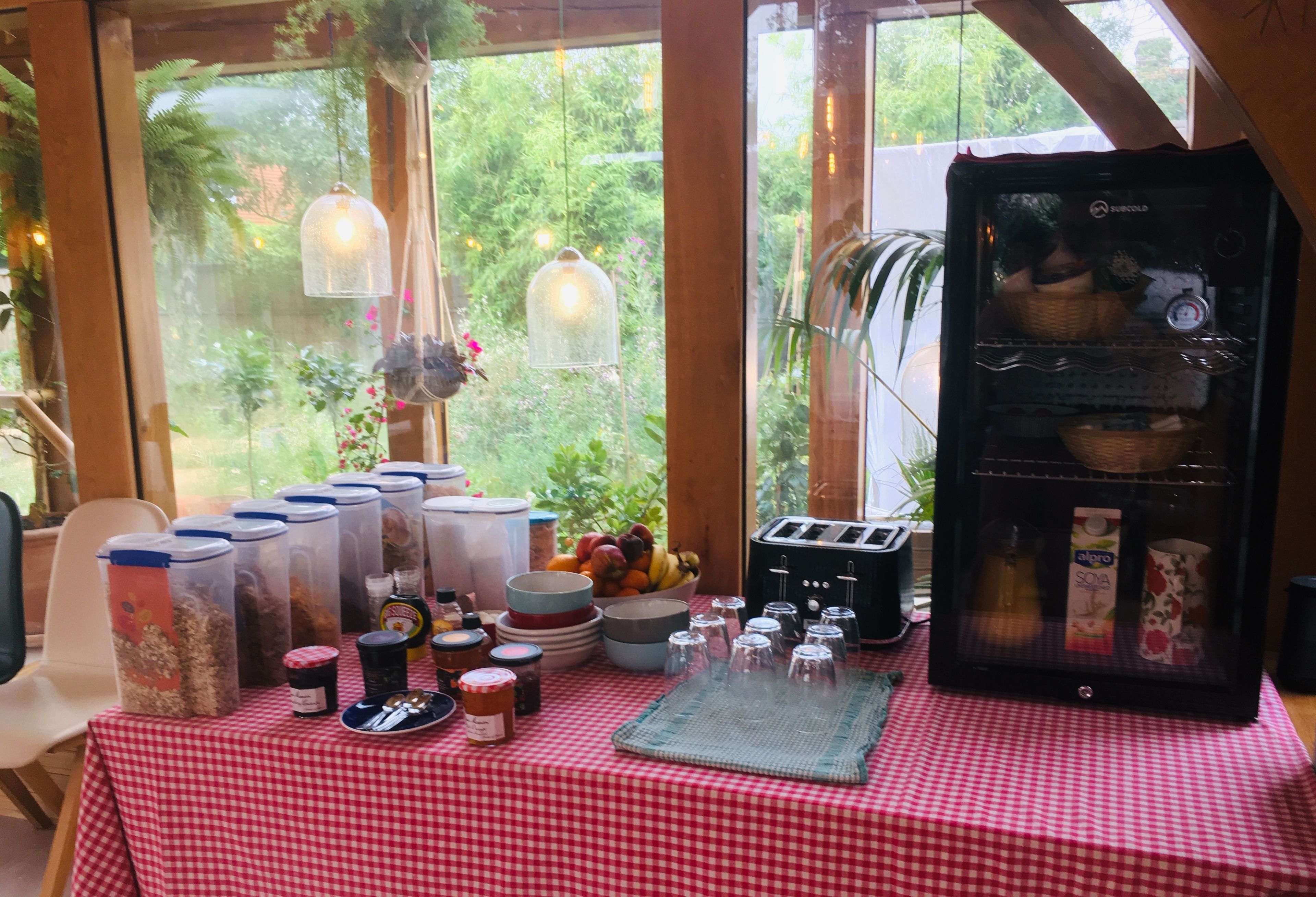Uma mesa com potes, uma torradeira e uma geladeira em um quarto com janelas amplas e luminárias penduradas.