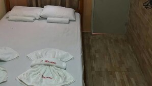 Quarto de hotel com cama, cabeceira de madeira, porta com placa e piso de azulejos.