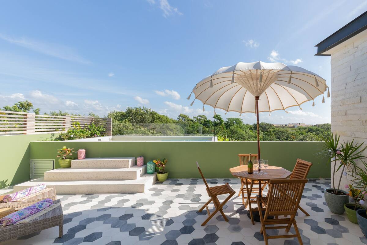 Terraço no telhado com mesa, cadeiras, um grande guarda-sol e plantas em vasos.