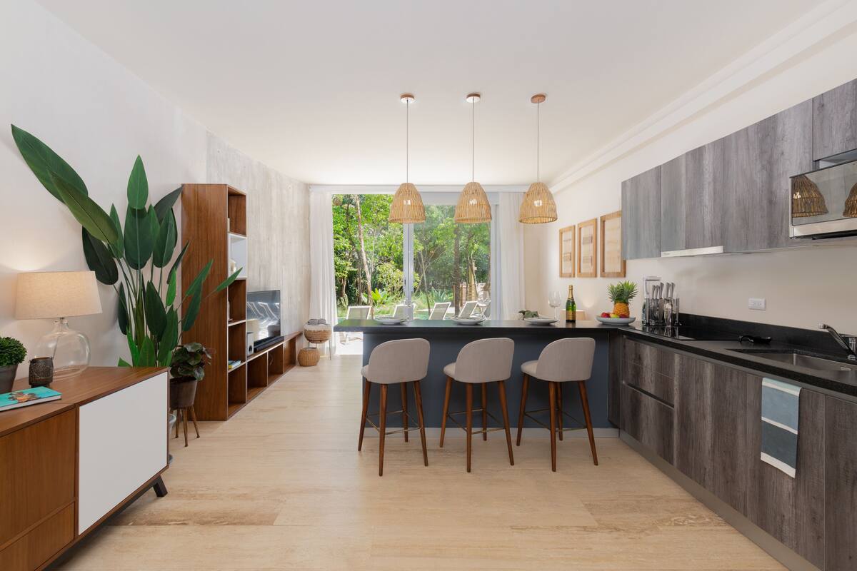 Cozinha moderna com ilha central, banquetas, iluminação pendente e vista para o verde lá fora.