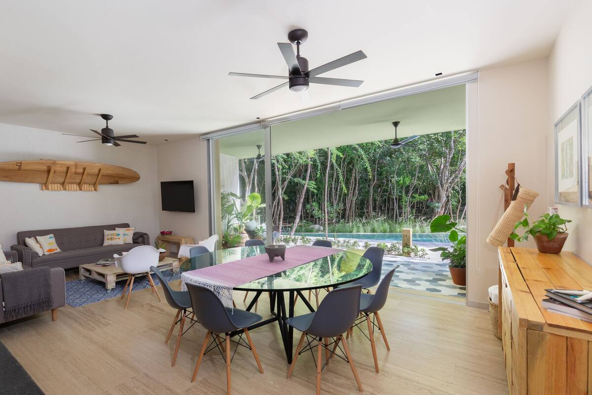 Uma sala de estar moderna com uma mesa de jantar de vidro, sofá cinza e ventiladores de teto.