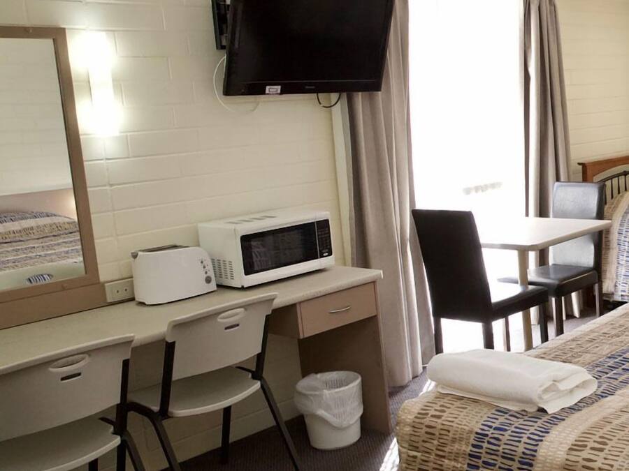Quarto de hotel com uma cama, uma escrivaninha equipada com micro-ondas, televisão na parede e janela com cortinas.