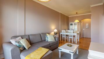 Uma sala de estar com um sofá cinzento, uma mesa de centro branca e uma área de jantar com cadeiras e mesa brancas.