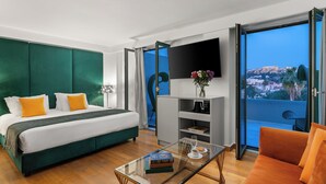 Quarto de hotel moderno com uma cama grande, um sofá, uma TV e uma varanda com vista para a cidade.