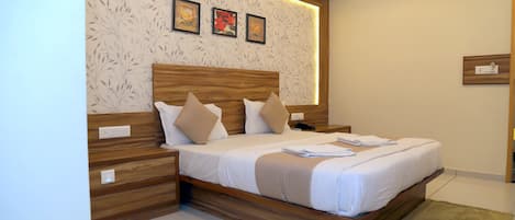 Quarto moderno com cabeceira de madeira, uma cama grande com roupa de cama branca, mesa de cabeceira e luminária fixada na parede.