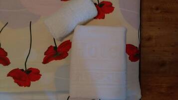 Toalha branca e travesseiro branco com estampas de flores vermelhas sobre superfície bege.