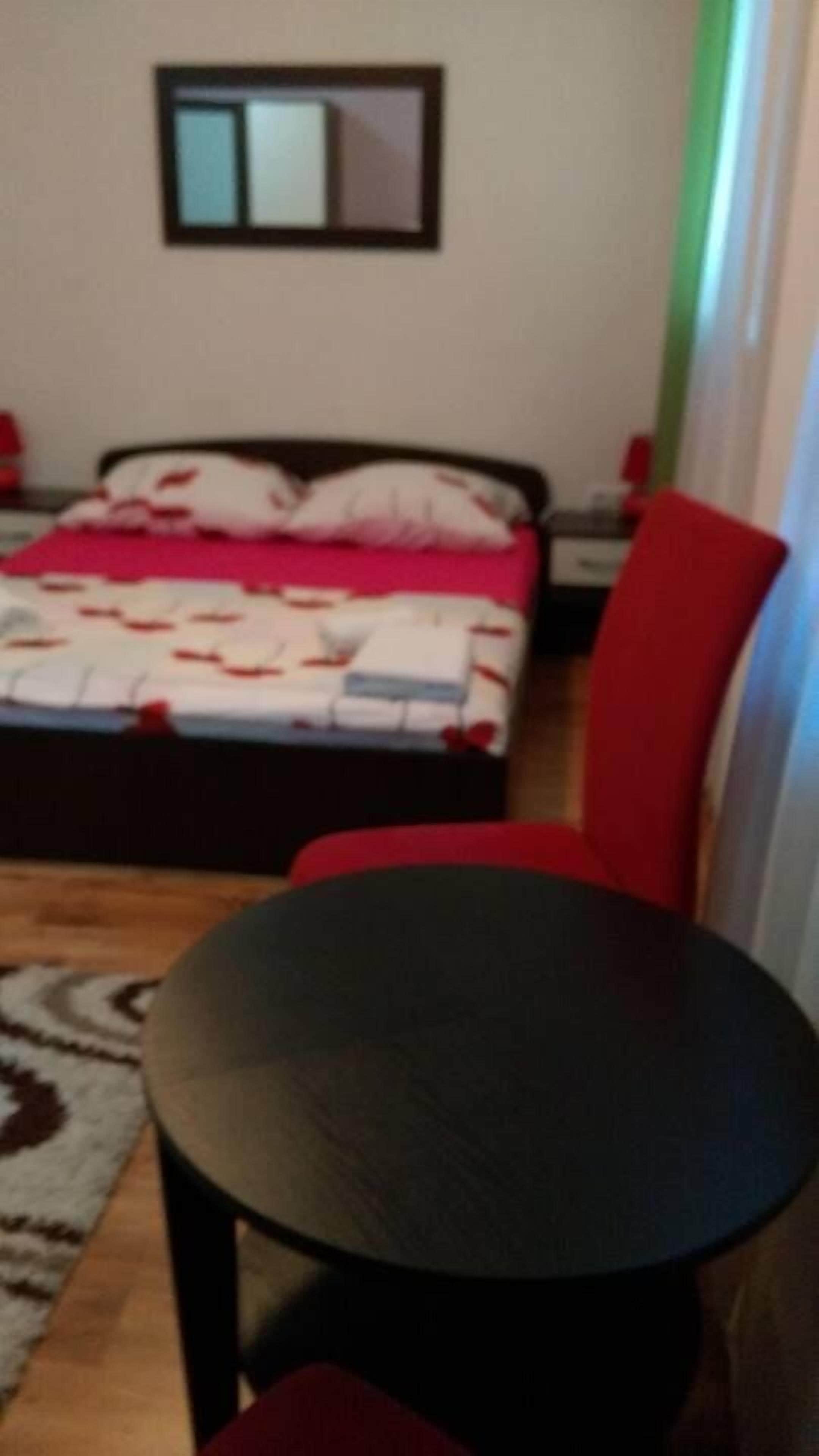 Um quarto com uma cama, uma mesa de cabeceira, uma cadeira vermelha e uma pequena mesa.