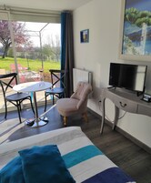 Quarto de hotel com uma cama, uma escrivaninha e televisão, uma cadeira e uma mesa com cadeiras.