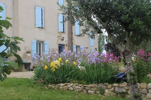 Um edifício com persianas azuis, uma parede de pedra e um jardim com diversas flores.
