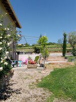 Área de pátio com assentos externos, um pequeno jardim e vista para um vinhedo.