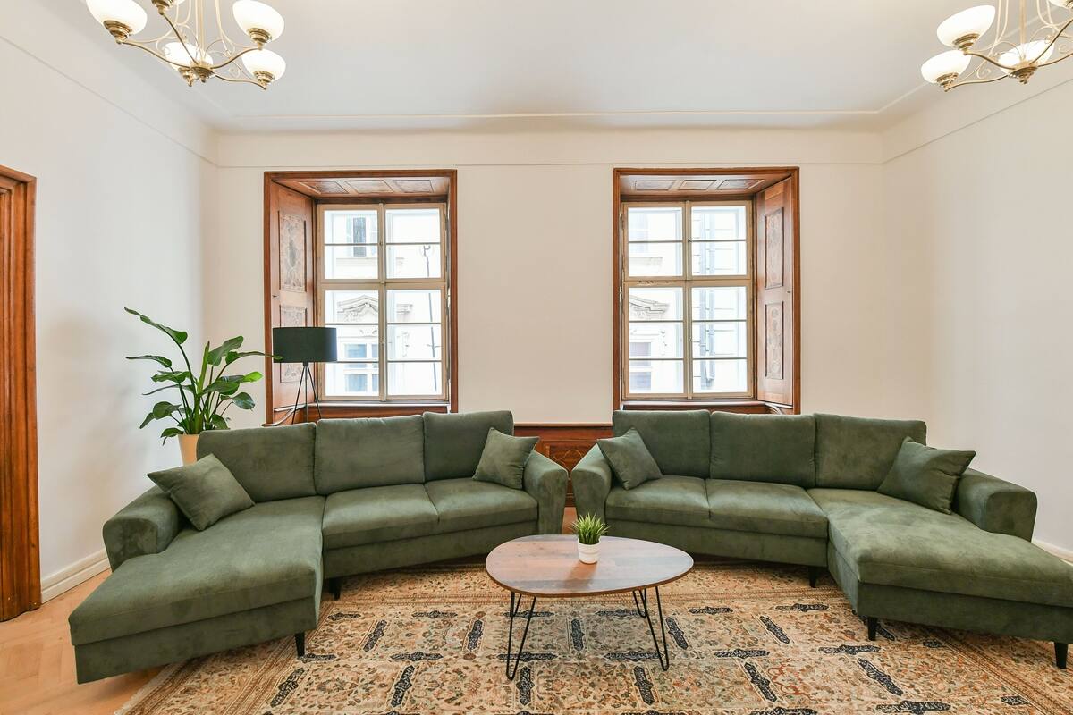 Uma sala de estar com um sofá seccional verde, uma mesa de centro redonda e um tapete estampado.
