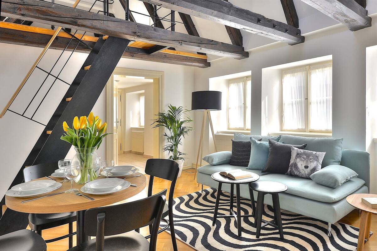 Uma sala de estar moderna com área de jantar, apresentando uma escada, um conjunto de sofá, um abajur e um vaso de planta.