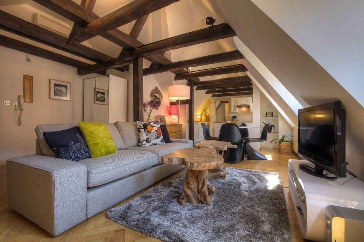 Uma sala de estar aconchegante com um sofá cinzento, mesa de centro de madeira e uma televisão.