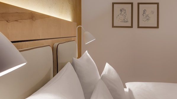 Quarto de hotel com cabeceira de madeira, roupa de cama branca e duas obras de arte emolduradas na parede.