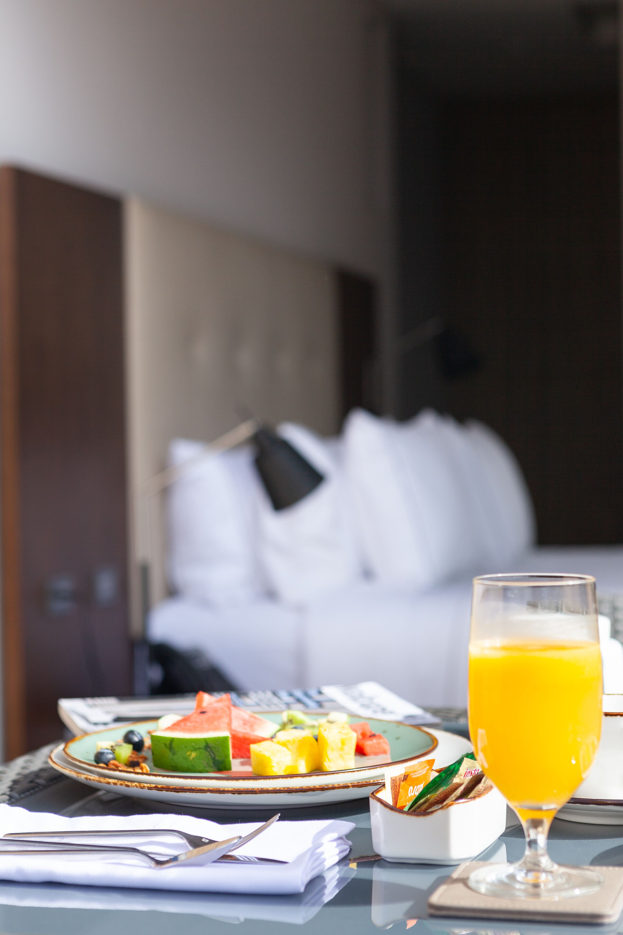 Uma mesa de café da manhã com uma travessa de frutas, um copo de suco de laranja e um pequeno recipiente com lanches.
