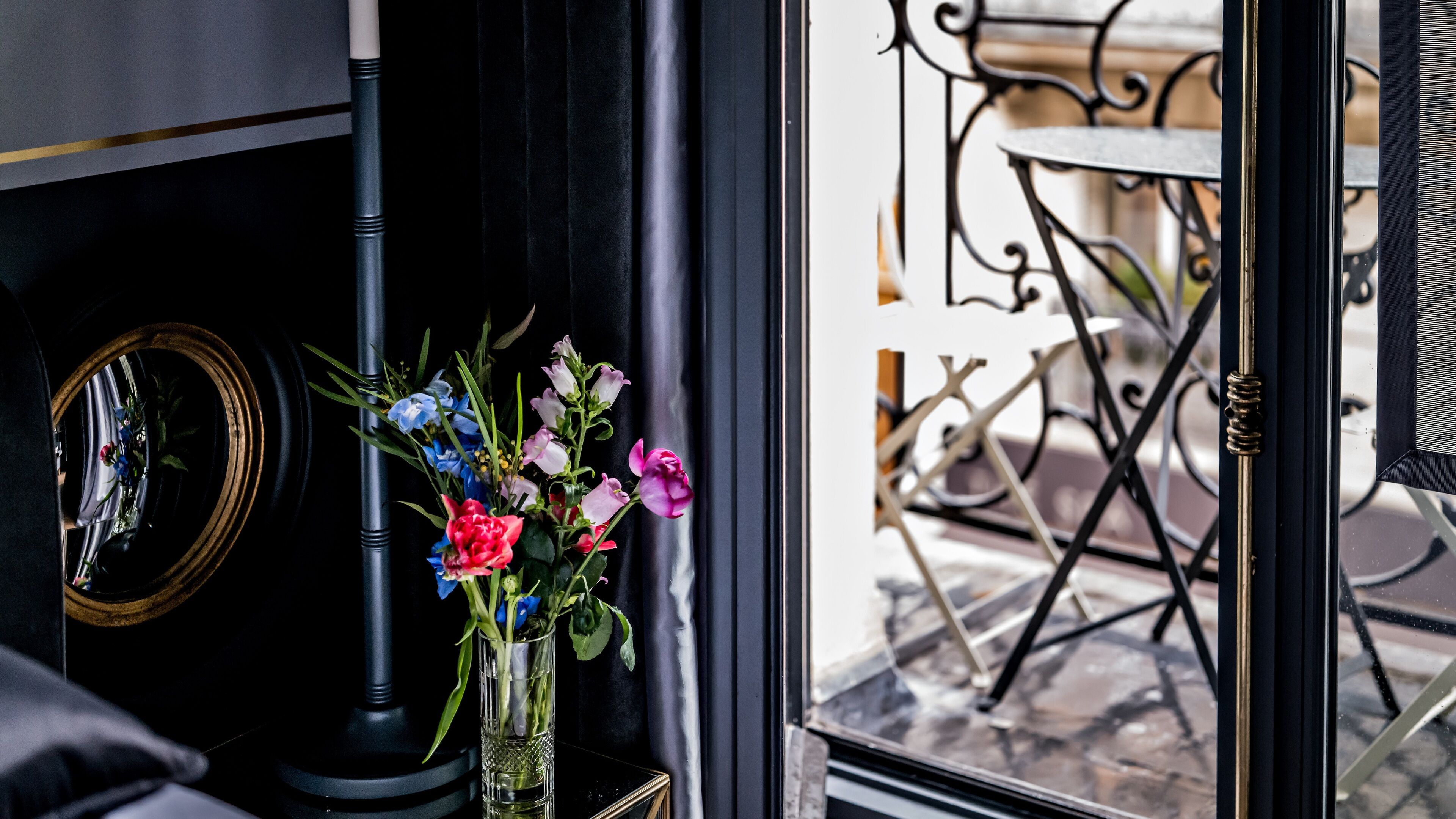 Janela com vista para um pátio externo, um vaso com flores e um espelho refletindo parte do quarto.