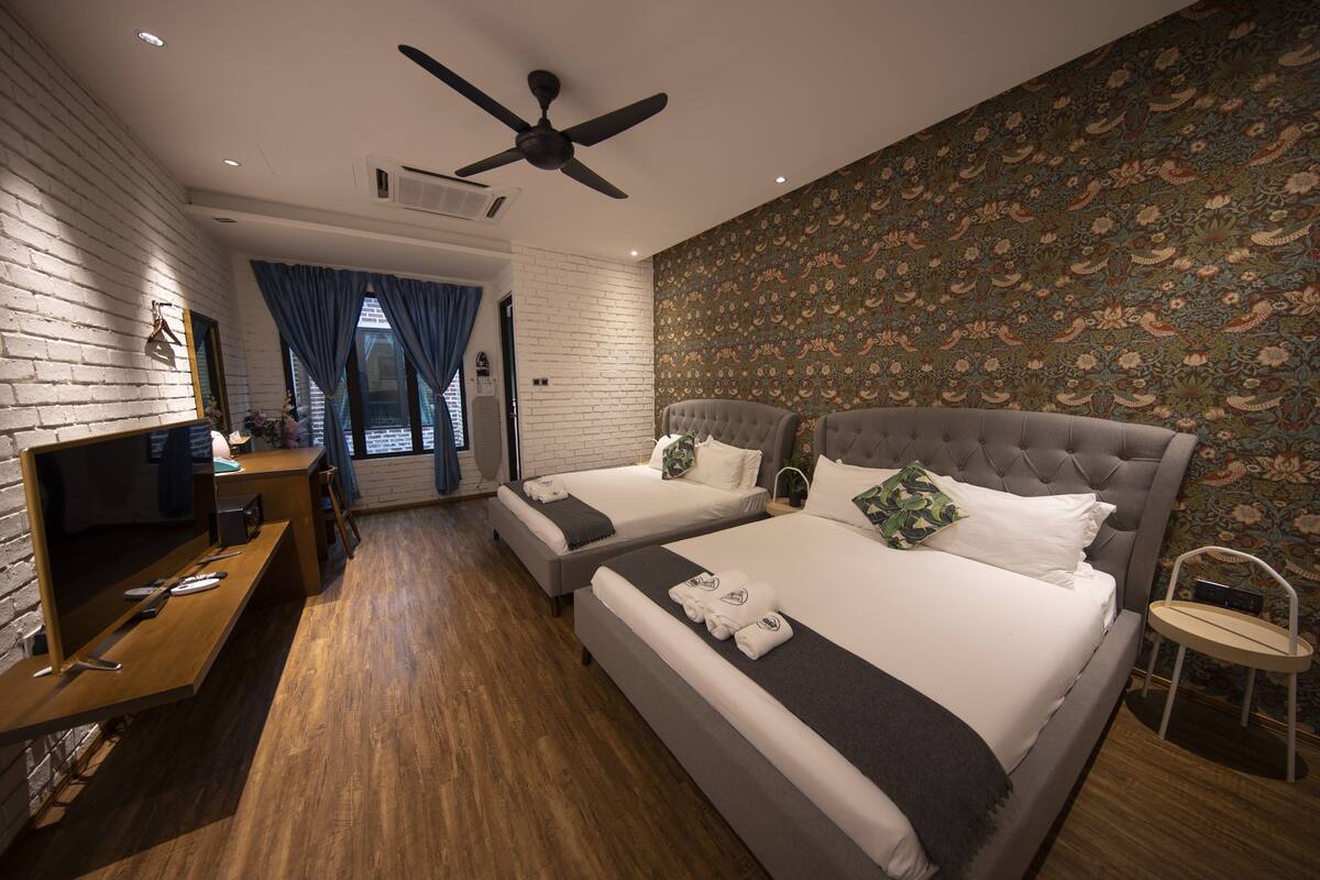 Quarto de hotel com duas camas, televisão, escrivaninha e ventoinha no teto.
